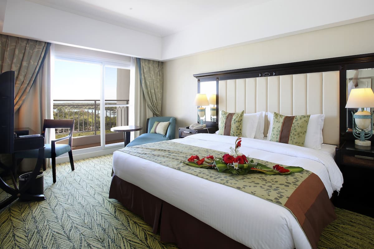 Quarto de hotel com uma cama grande, uma mesa, uma cadeira e varanda com vista.