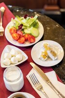 Uma mesa com uma salada, um prato de bolinhas de mussarela, um prato com um prato de peixe, um copo de leite e talheres.
