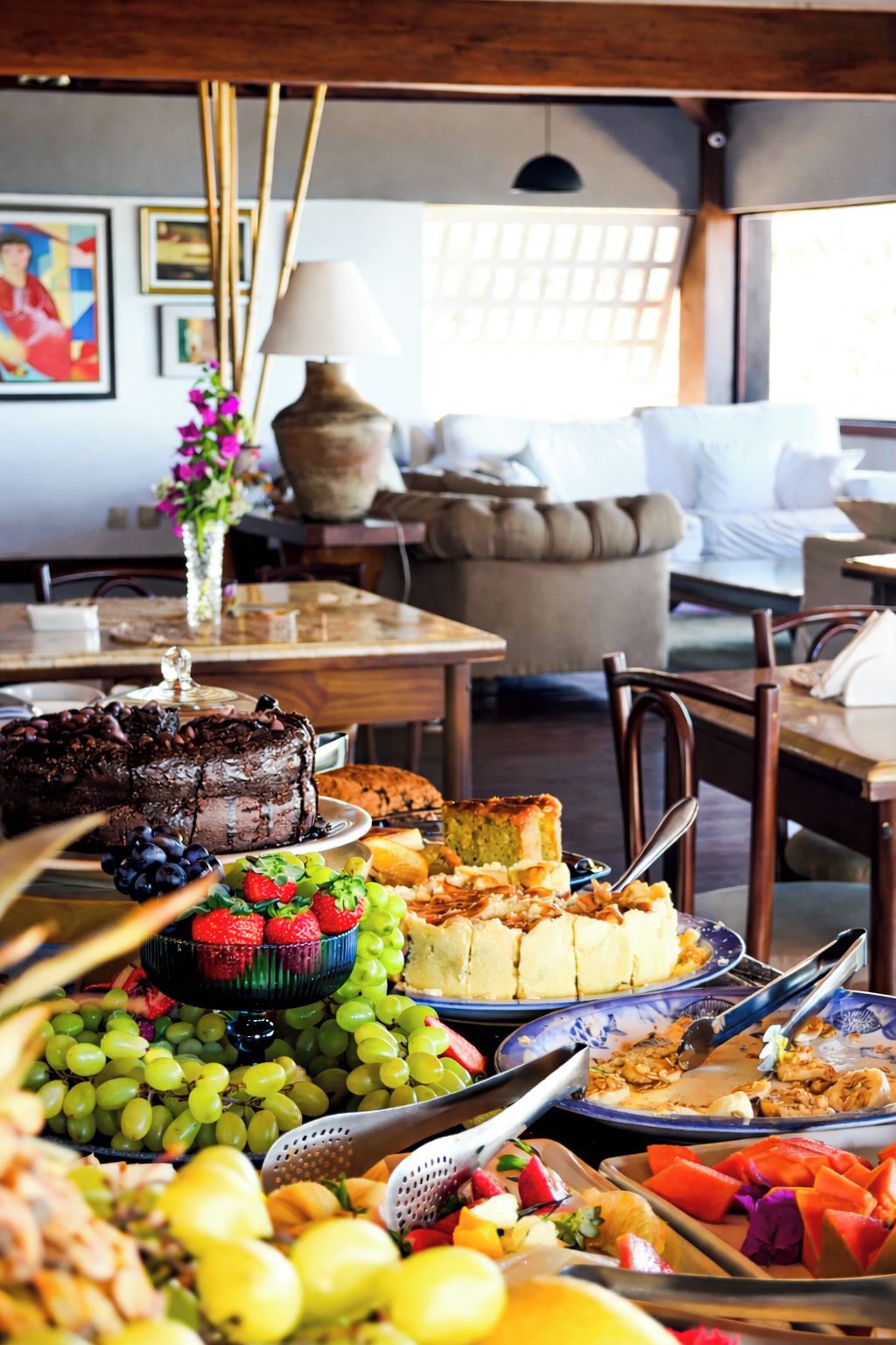 Uma área de refeições com diversos alimentos, incluindo um bolo de chocolate, frutas e uma travessa de doces.