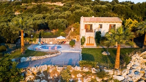 Uma vila de pedra com piscina, rodeada por vegetação exuberante e palmeiras.