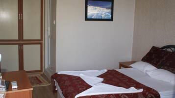 Quarto de hotel com cama, mesa de cabeceira de madeira, escrivaninha com telefone e quadro na parede.