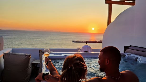 Um casal relaxando em uma banheira de hidromassagem com vista para o pôr do sol.