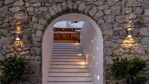 Escadaria que leva a um deck de madeira, ladeada por paredes de pedra com iluminação embutida.
