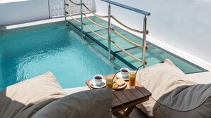 Piscina com barreira de vidro, espreguiçadeiras e uma mesa com bebidas e um prato de comida.
