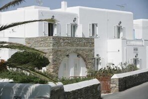 Um edifício branco com entrada em arco de pedra, um pequeno jardim e um espaço pavimentado na frente.