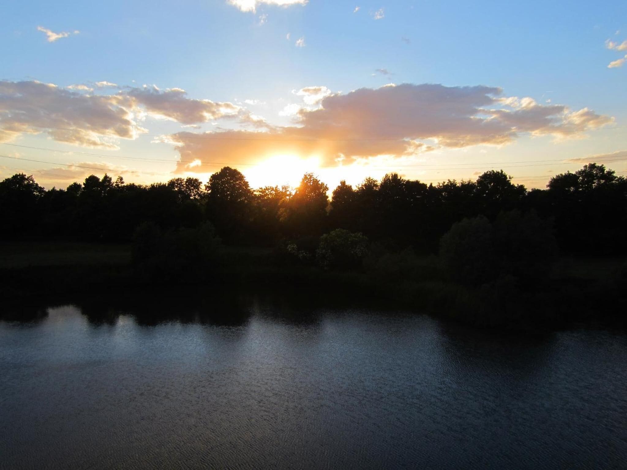 Um pôr do sol sobre um lago calmo, com árvores ao fundo.