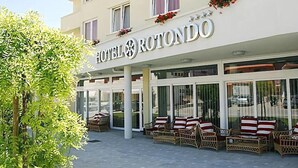 Exterior de um hotel com uma placa indicando "HOTEL ROTO NDO". Há cadeiras de vime com almofadas listradas em frente à entrada.