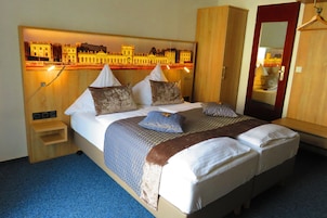 Quarto de hotel com uma cama grande, cabeceira com vista para a cidade, mesa de cabeceira de madeira e um espelho na parede.