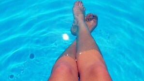 Pernas de alguém em uma piscina com água azul cristalina.