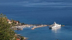 Uma marina com um iate branco grande atracado num cais, rodeado por barcos menores e uma cidade costeira com edifícios e vegetação.