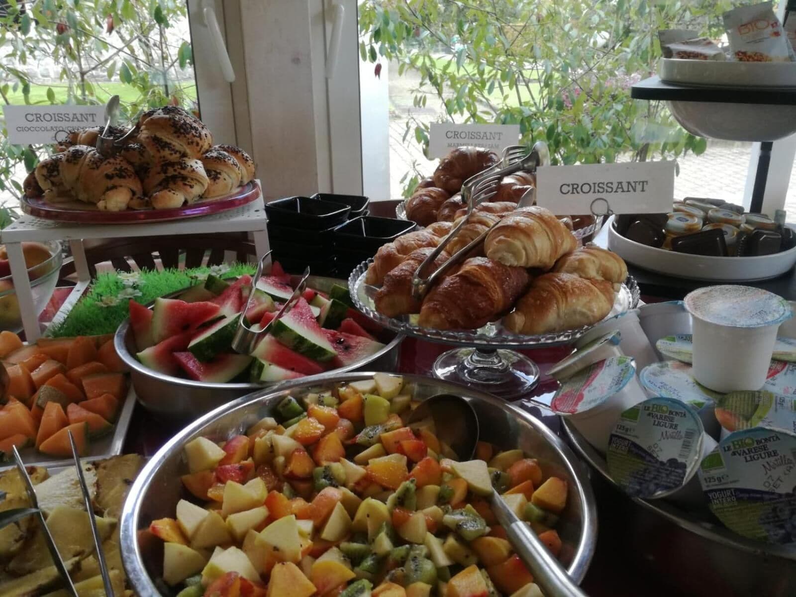 Buffet com croissants, melancia e uma variedade de frutas e vegetais.