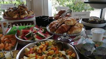 Buffet com croissants, melancia e uma variedade de frutas e vegetais.