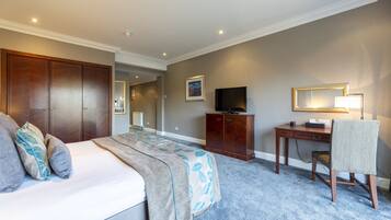 Quarto de hotel com cama, escrivaninha, cadeira, guarda-roupa, televisão e um quadro na parede.