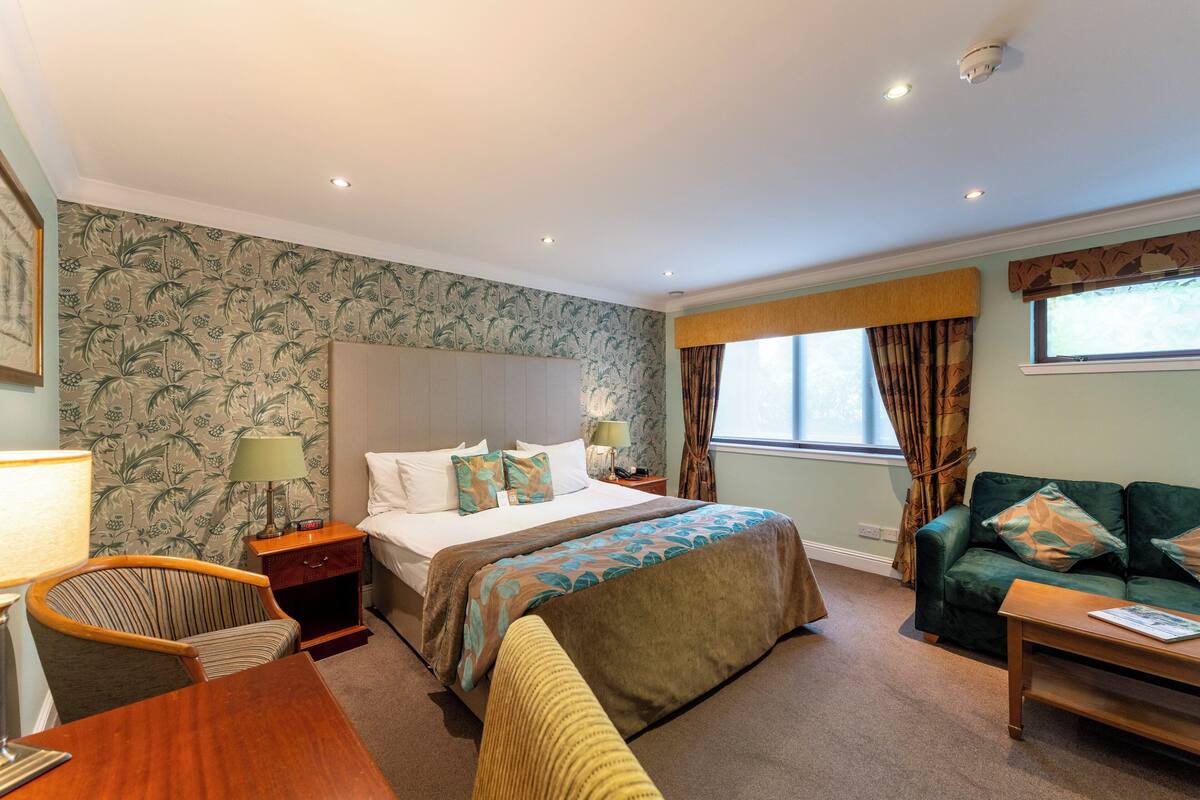 Quarto de hotel com cama, sofá, escrivaninha e cadeira.