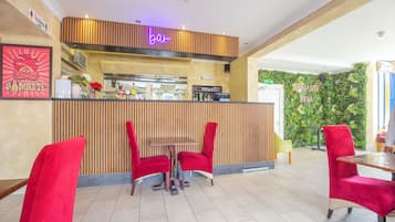 Uma área de bar com balcão de madeira, cadeiras vermelhas e parede verde com plantas.