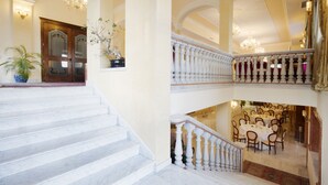 Uma escadaria imponente conduz a uma sala de jantar com pisos de mármore e um candelabro.