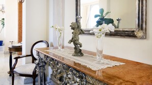 Uma sala de jantar com uma mesa de mármore, cadeiras elaboradas, um espelho decorativo e flores brancas sobre a mesa.