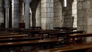 Interior de igreja com arcos de pedra e bancos de madeira.