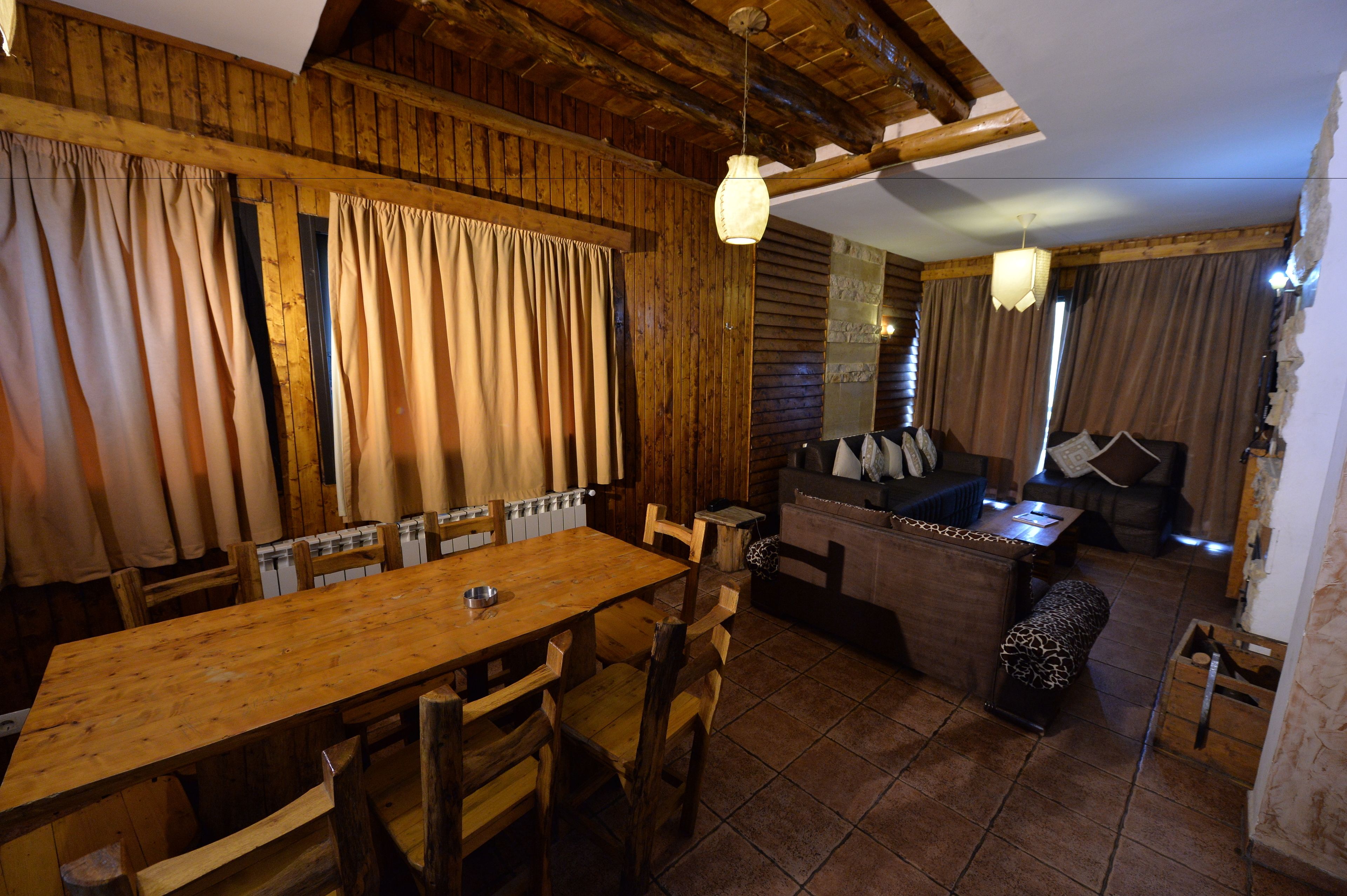 Um interior rústico de madeira com uma mesa de jantar, cadeiras, um sofá e uma pequena cozinha.