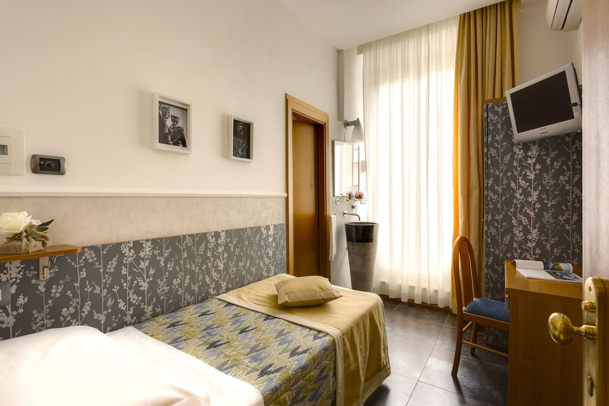 Quarto de hotel com duas camas, uma escrivaninha, uma cadeira, uma televisão e um banheiro.