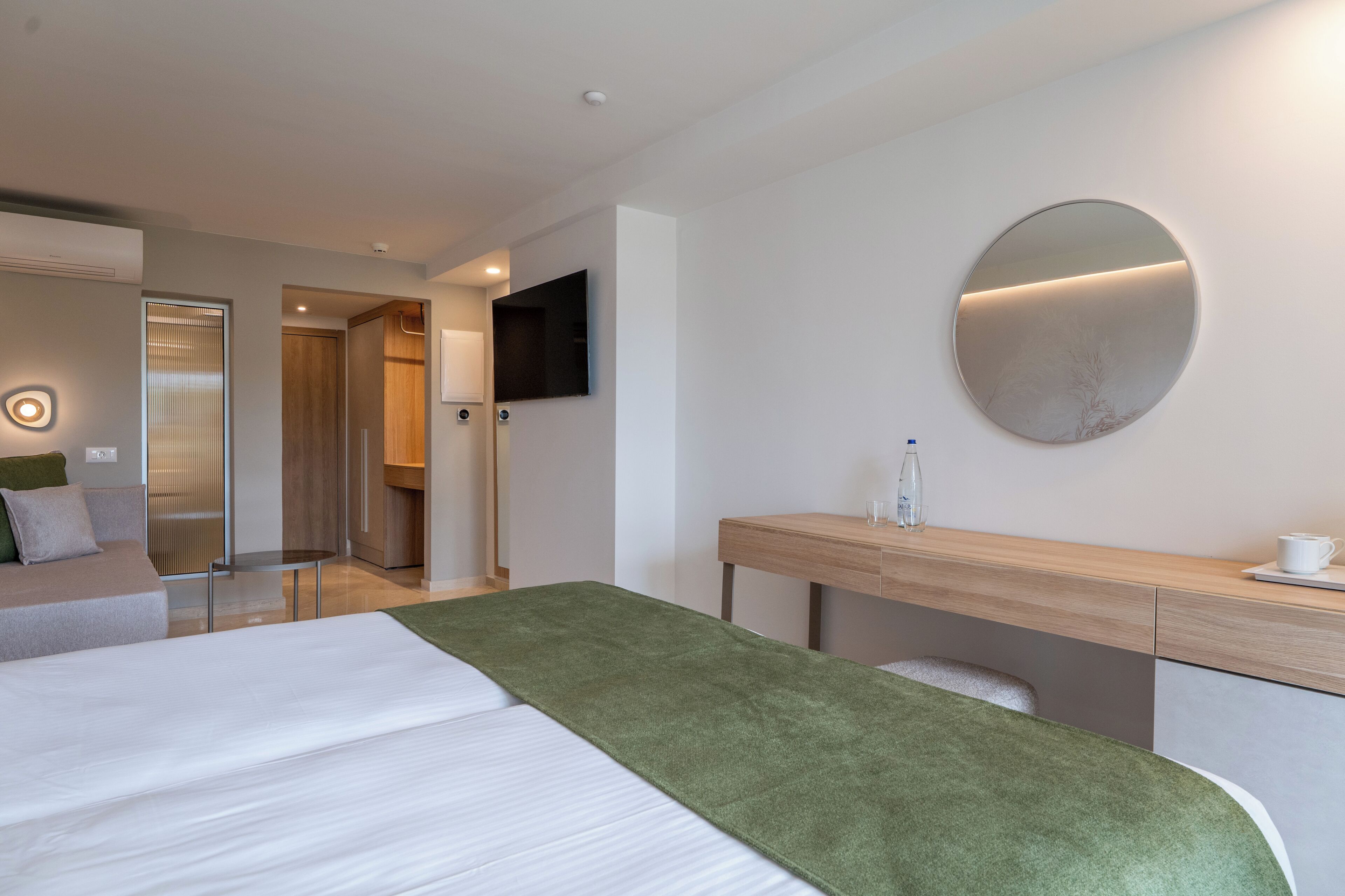 Quarto de hotel moderno com cama, escrivaninha, espelho e televisão.