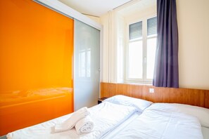 Quarto de hotel com cama, janela com cortinas e uma parede laranja vibrante.