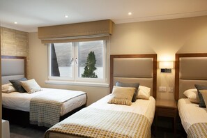 Quarto de hotel com duas camas de solteiro, uma janela grande com vista, cabeceira de madeira e luminária de cabeceira.