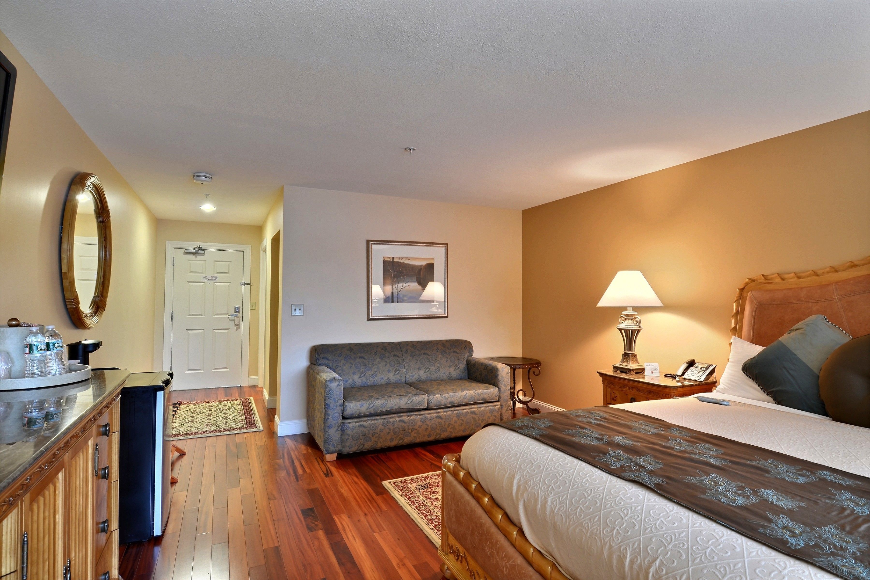 Quarto de hotel com cama, sofá, escrivaninha com luminária e um quadro na parede.