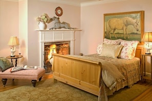 Quarto com cama de madeira, lareira, pintura de um cavalo e relógio na parede.