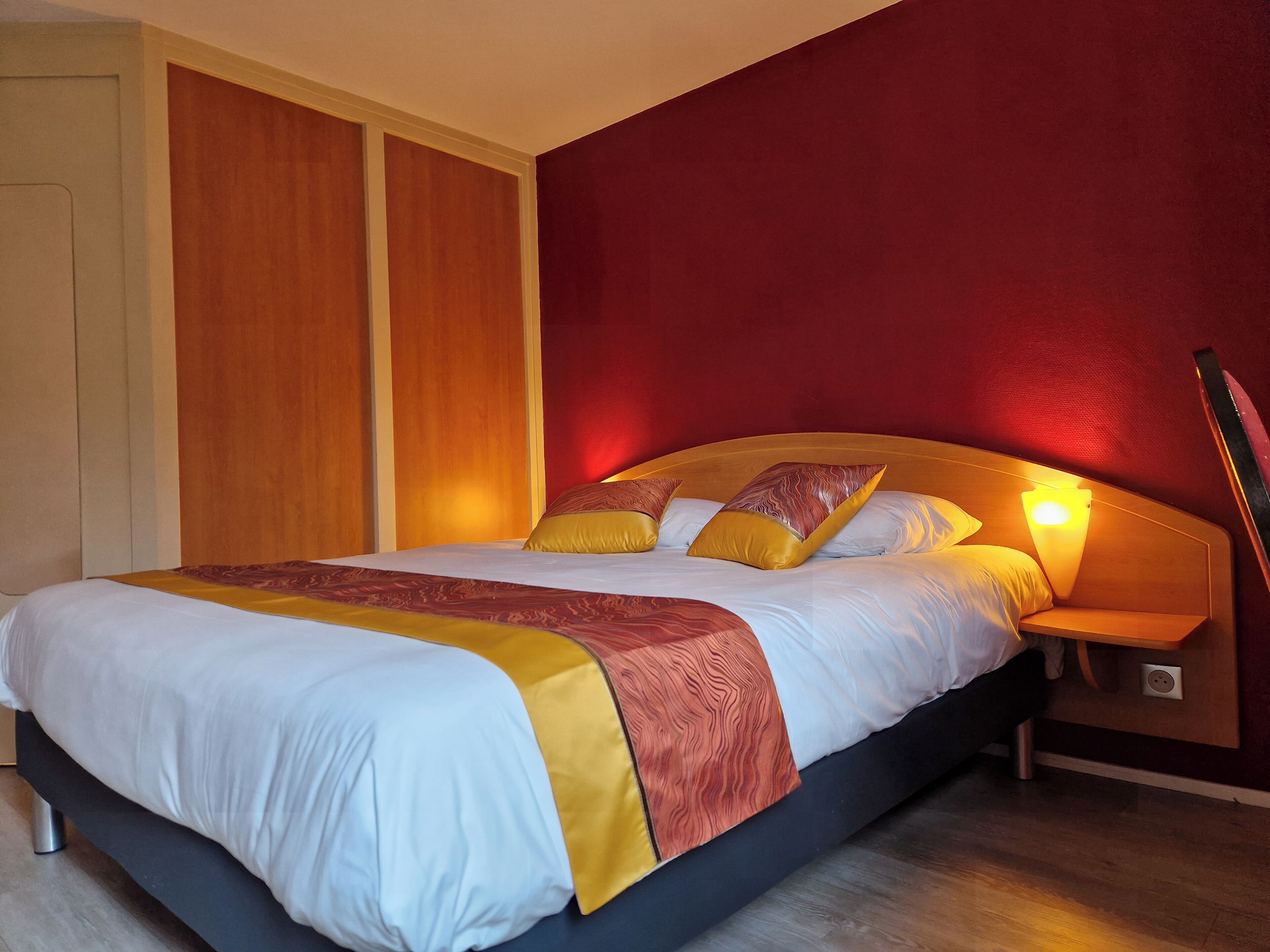 Quarto de hotel com cama grande, cabeceira de madeira e parede com destaque em vermelho.