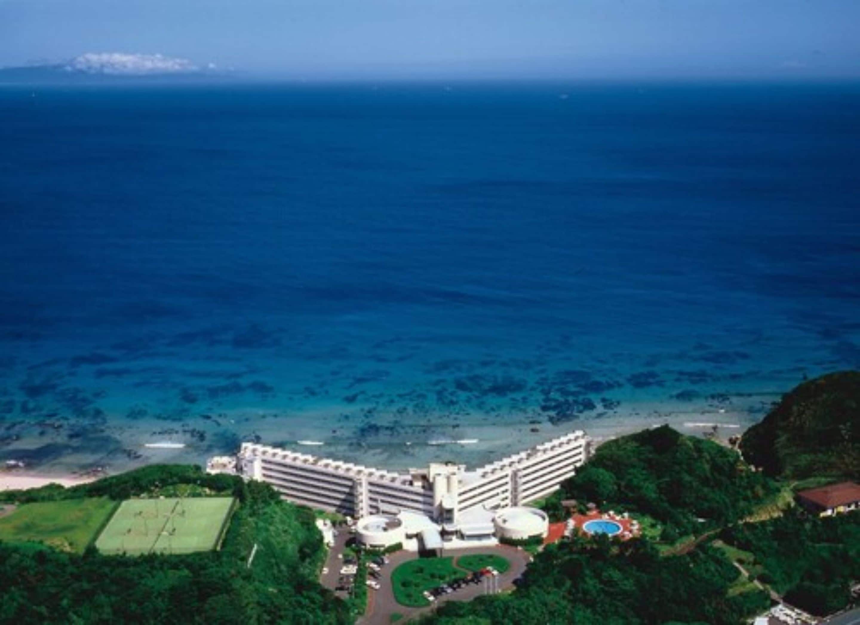 Um grande hotel com várias construções, praia e vista clara do oceano.