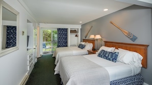 Quarto de hotel com duas camas, cabeceira de madeira, mesa de cabeceira, luminária, janela com cortinas e porta que dá para uma varanda.