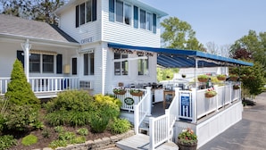 Um edifício branco com toldo azul, um deck com jardineiras de flores penduradas e uma placa indicando uma cafeteria.
