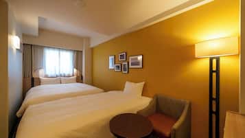 Quarto de hotel com duas camas, uma mesa redonda pequena, uma cadeira e um abajur.