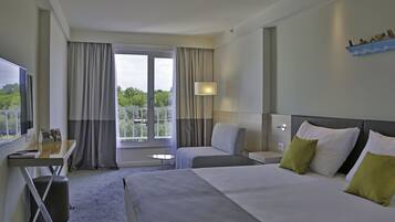 Quarto de hotel com uma cama grande, uma escrivaninha, uma cadeira, uma mesinha e varanda com cortinas.