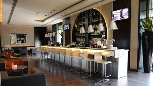 Uma área de bar moderna com um balcão comprido, vários bancos altos e uma tela de televisão na parede.