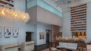 Um lobby moderno com balcão de recepção, área de estar, estantes de livros e plantas decorativas.
