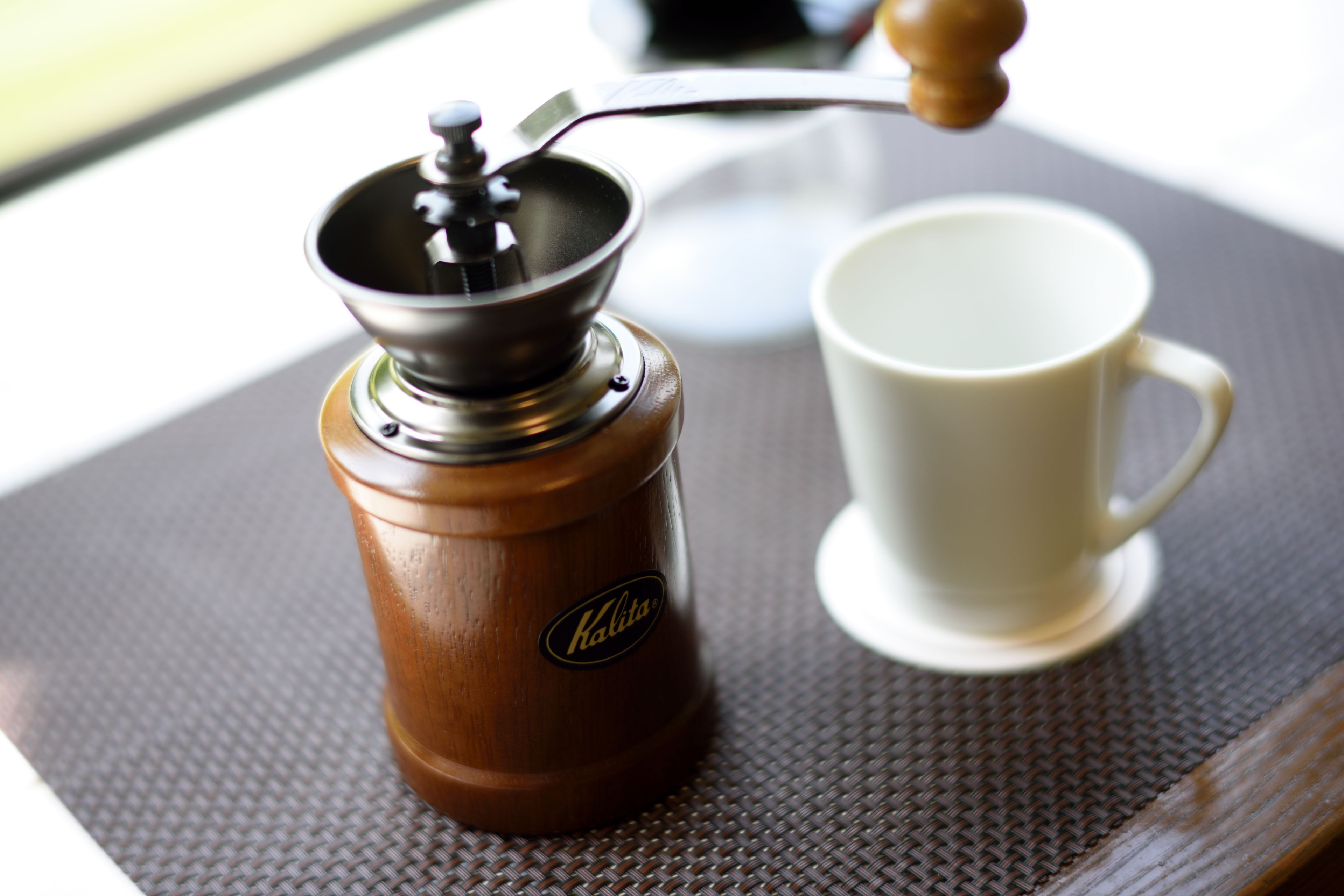 Moedor de café e uma xícara sobre um tapete texturizado.