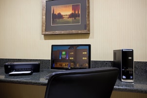 Quarto de hotel com um computador de mesa, impressora e um quadro na parede.