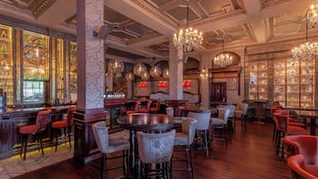 Uma área de bar com diversas opções de assento, incluindo banquetas e mesas redondas, e uma variedade de garrafas em exposição.