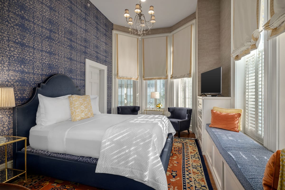 Quarto com cama grande, um banco, uma TV e um candelabro.