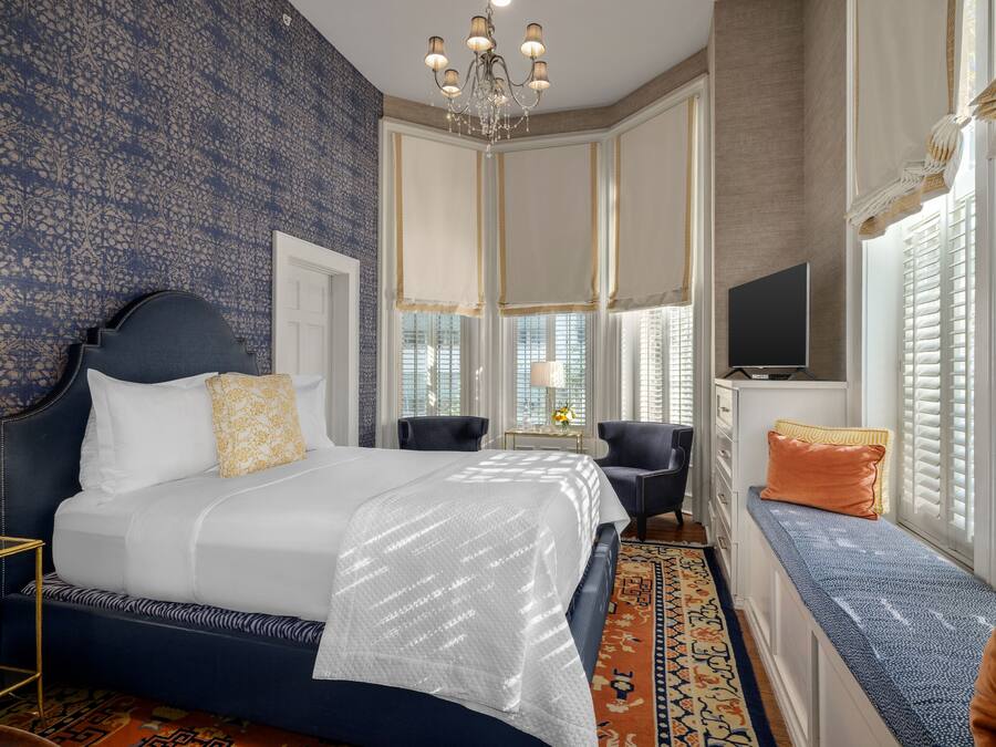 Quarto com cama grande, um banco, uma TV e um candelabro.