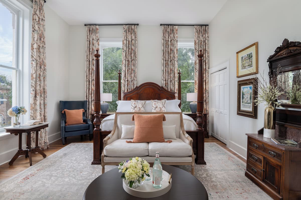 Quarto com uma cama grande, um sofá, uma mesa de centro com flores e um aparador.