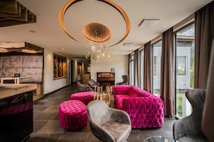 Interior moderno com área de estar, destacando sofás e pufes com capitonê, uma mesa de centro de madeira e uma luminária circular singular no teto.
