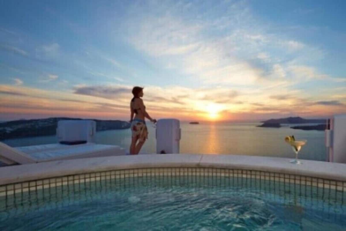 Uma pessoa em frente a uma piscina, com vista para o pôr do sol.
