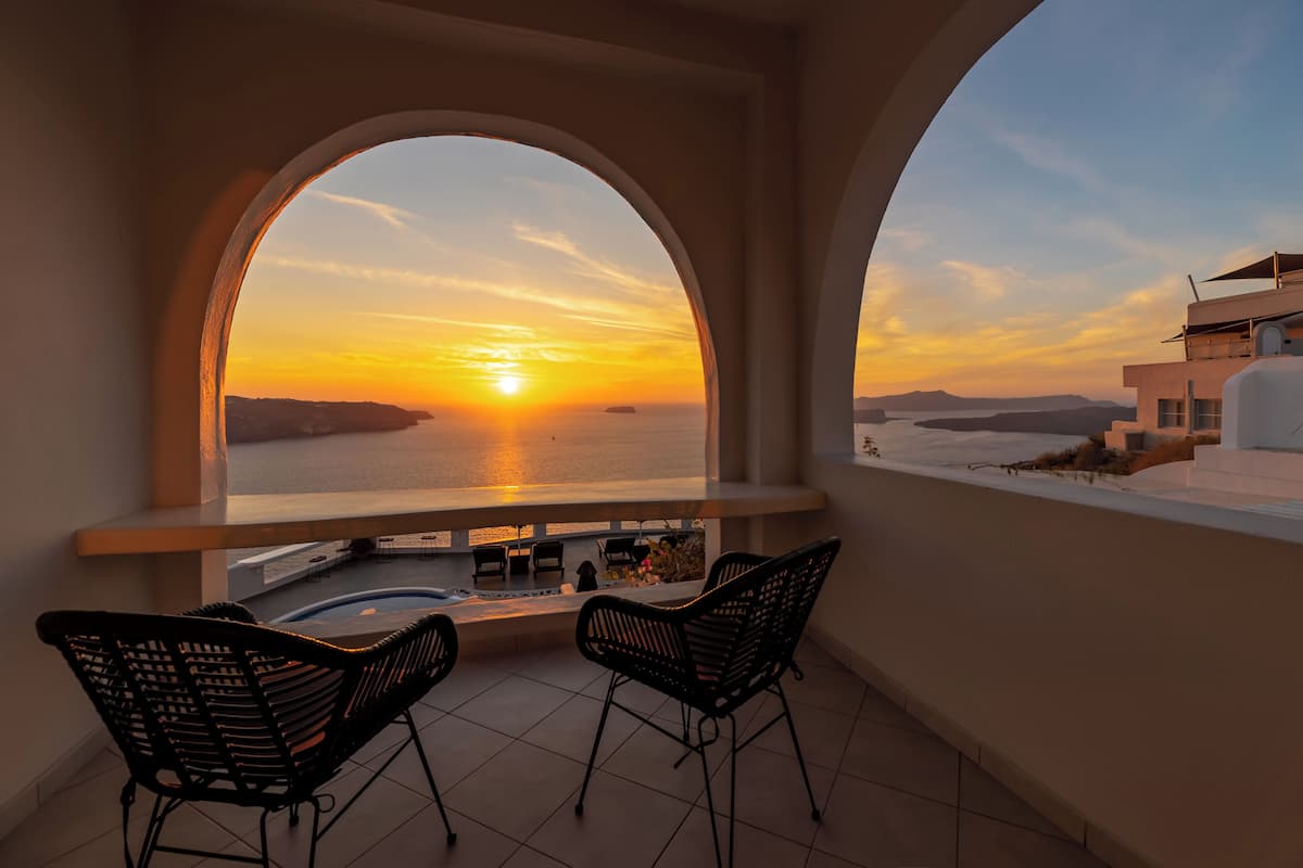 Varanda com duas cadeiras, piscina e vista para o pôr do sol sobre o mar.