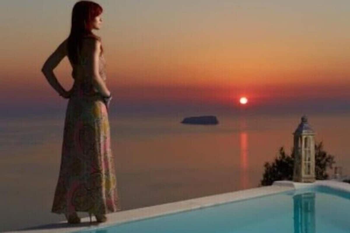 Mulher de pé perto de uma piscina com vista para o pôr do sol.