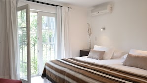 Quarto com cama grande, mesa de cabeceira, janela com cortinas e ar condicionado.