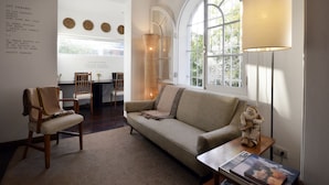 Uma sala de estar aconchegante com um sofá, cadeiras, uma luminária e uma mesa com livros.