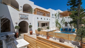 Pátio de hotel com piscina, bancos de madeira e plantas em vasos.